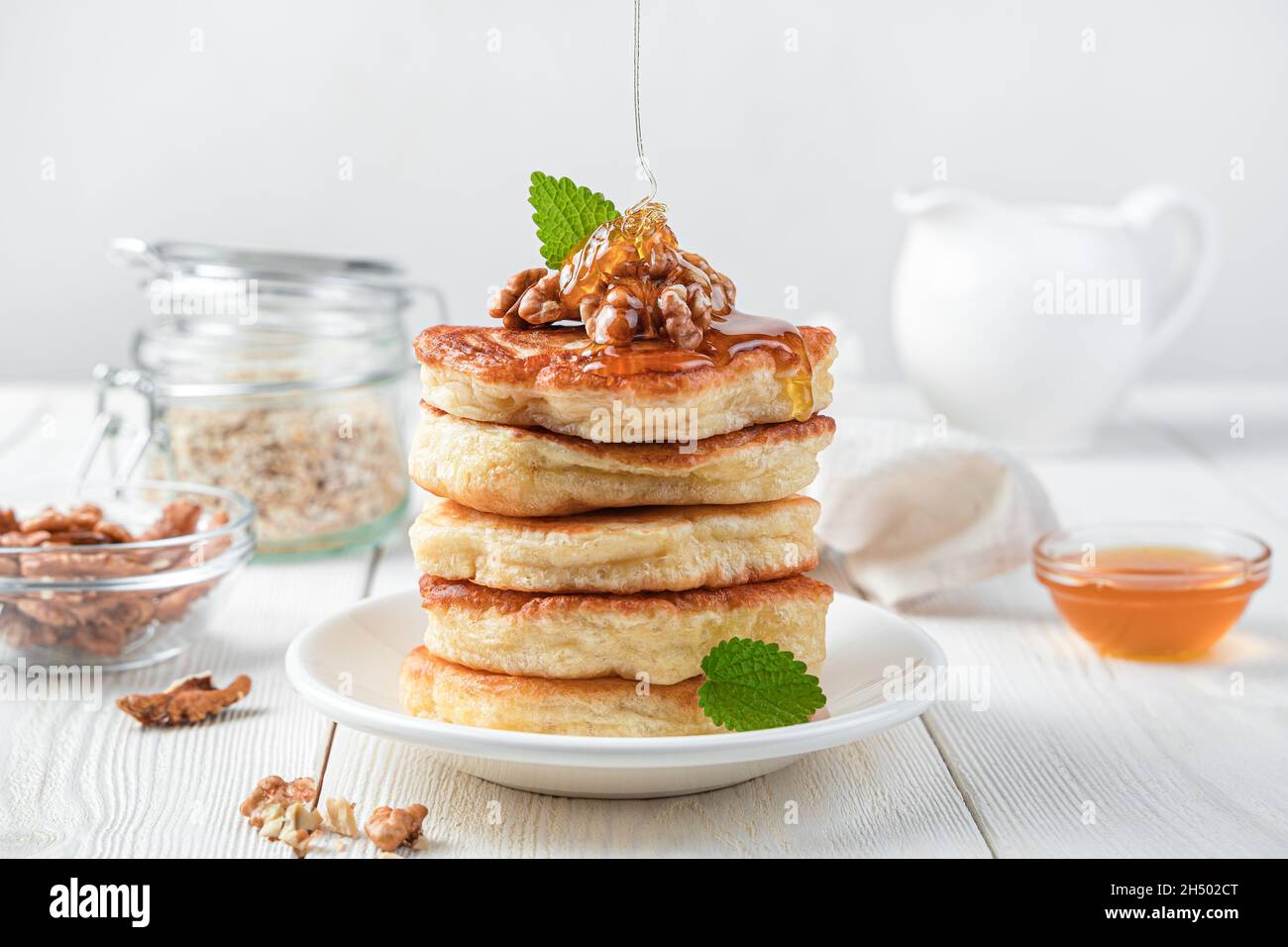 Pancakes with nuts and mint are pour with honey on a white background ...