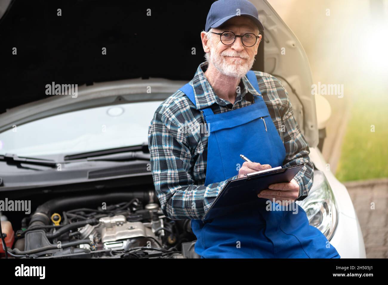 Car mechanic checking a car engine and writing on clipboard Stock Photo ...