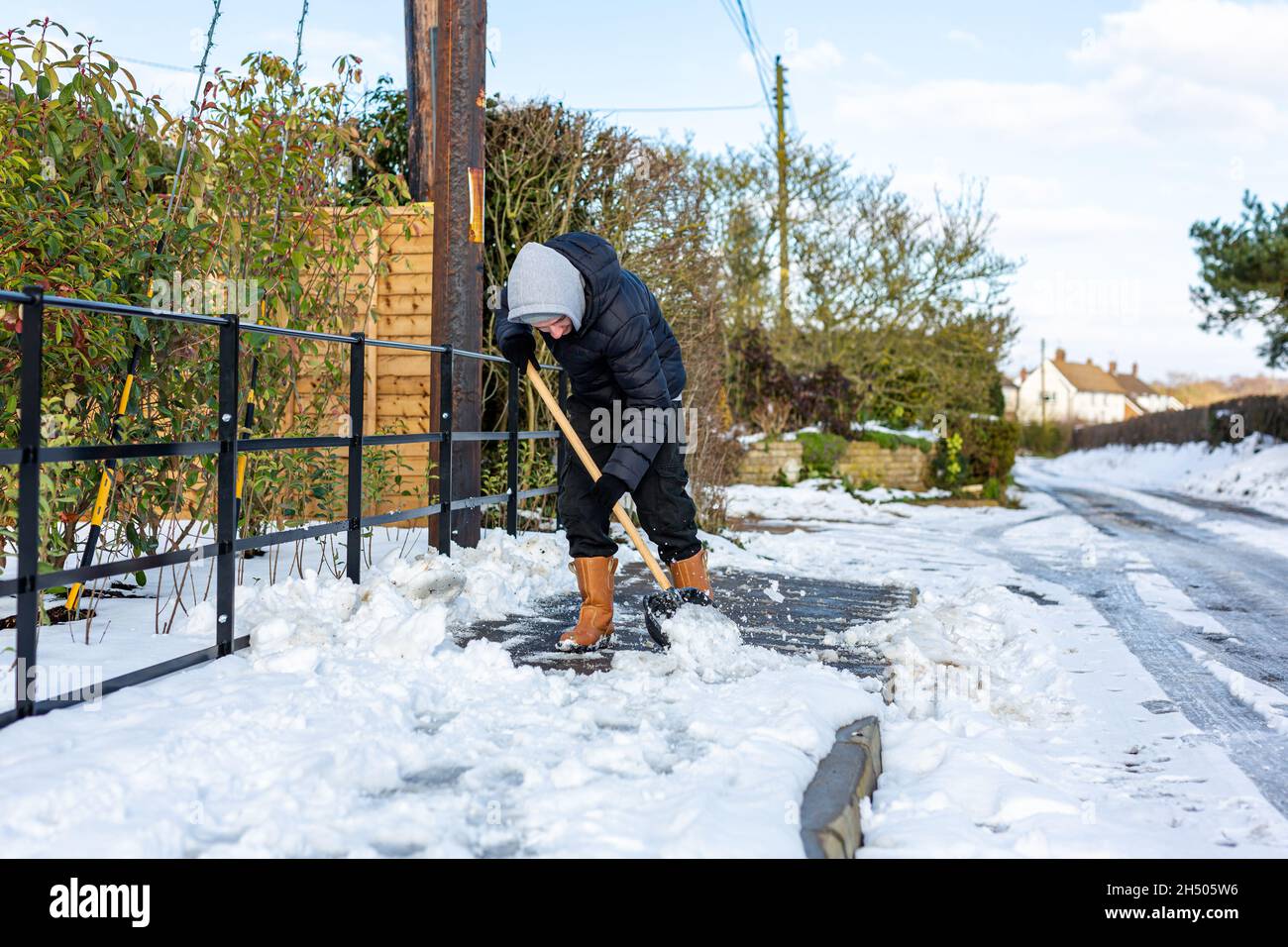 A young man clearing the footpath of snow and ice to make it safe to ...