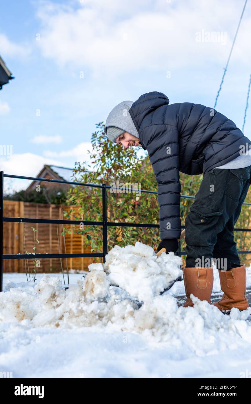 A young man clearing the footpath of snow and ice to make it safe to ...
