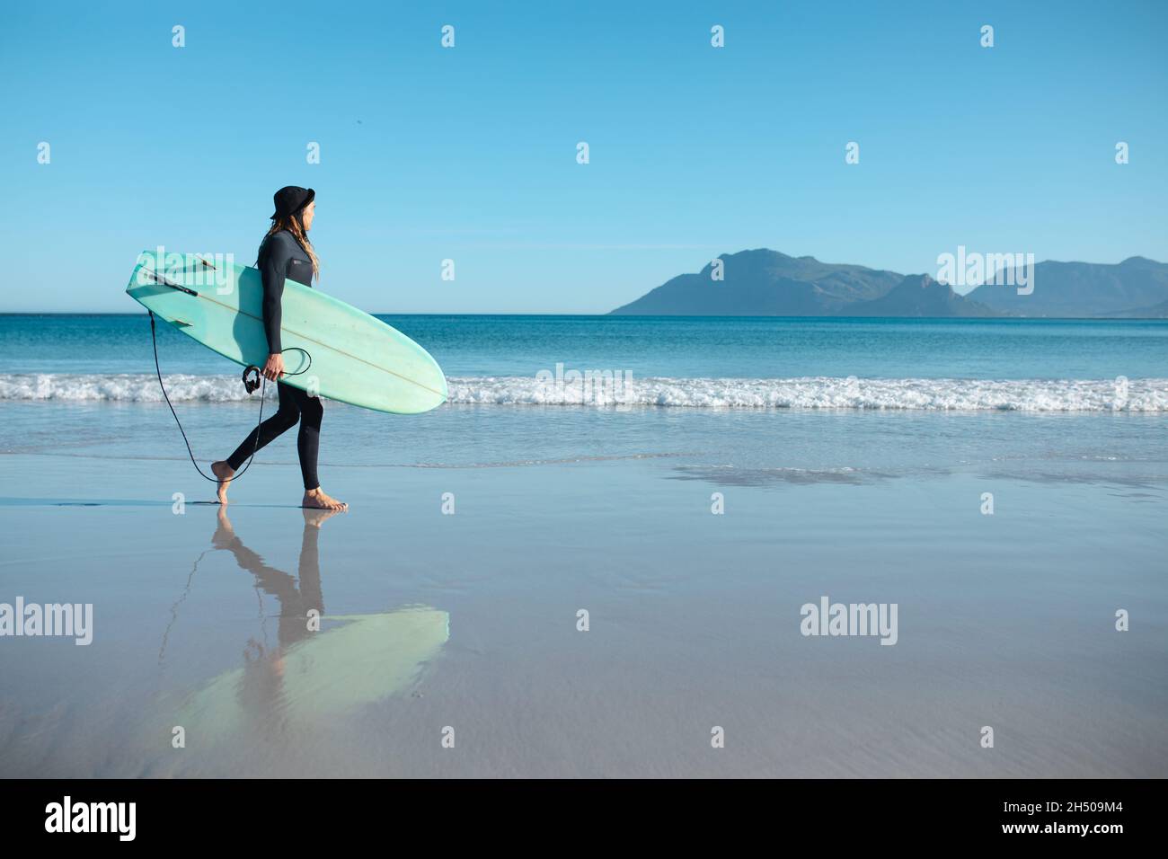 Side view of surfer carrying surfboard walking on shore while looking ...