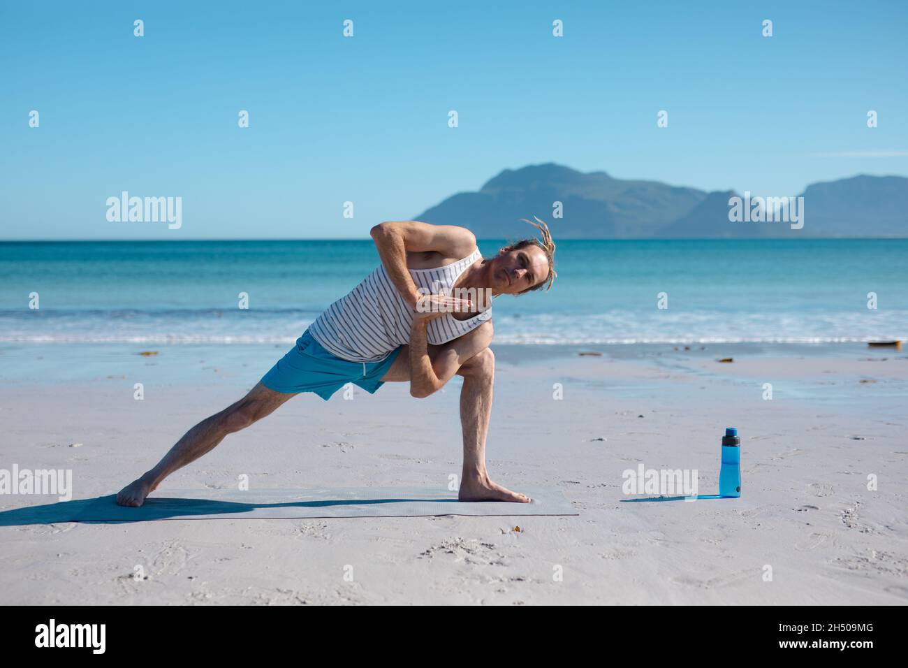 Full length of flexible man practicing yoga pose at beach against clear ...