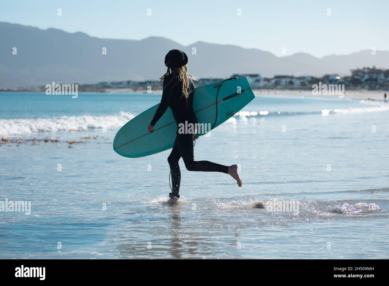Full length of male hipster running with surfboard on shore at beach ...