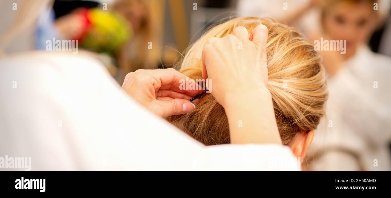 Hair stylist's hands doing professional hairstyling of female long hair ...