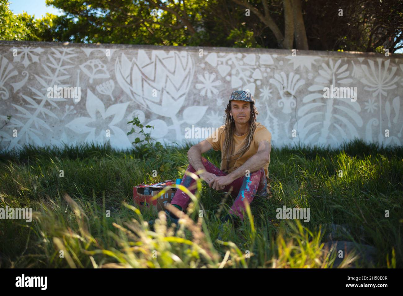Portrait of male artist sitting on grass against abstract mural ...
