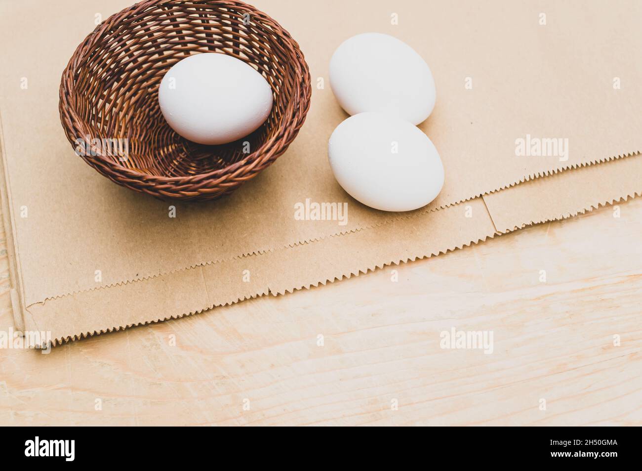 white eggs in a wicker canister on a wooden and brown paper background ...