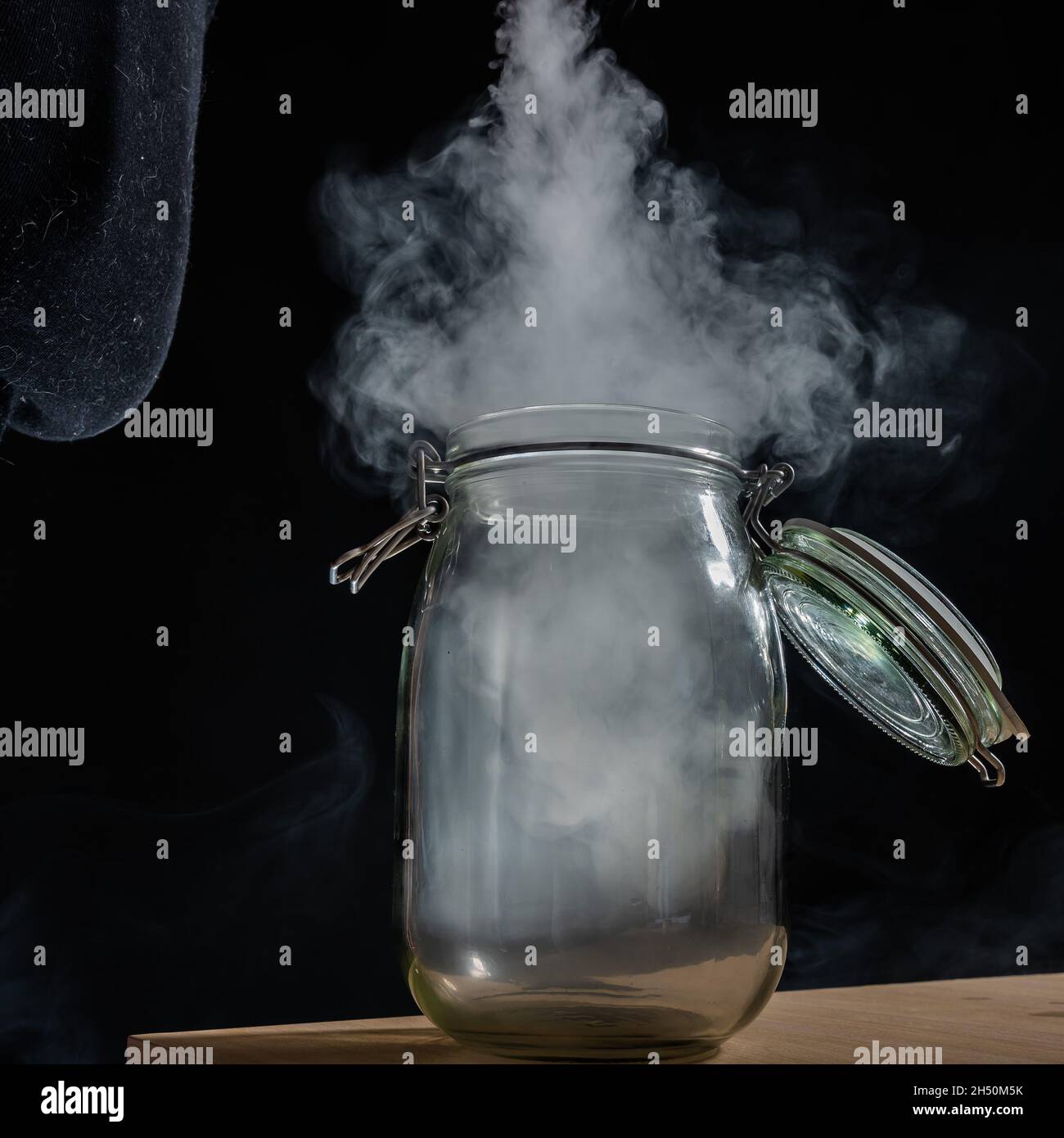 Glass jar with a lid filled with smoke on a black background. Fog in a ...