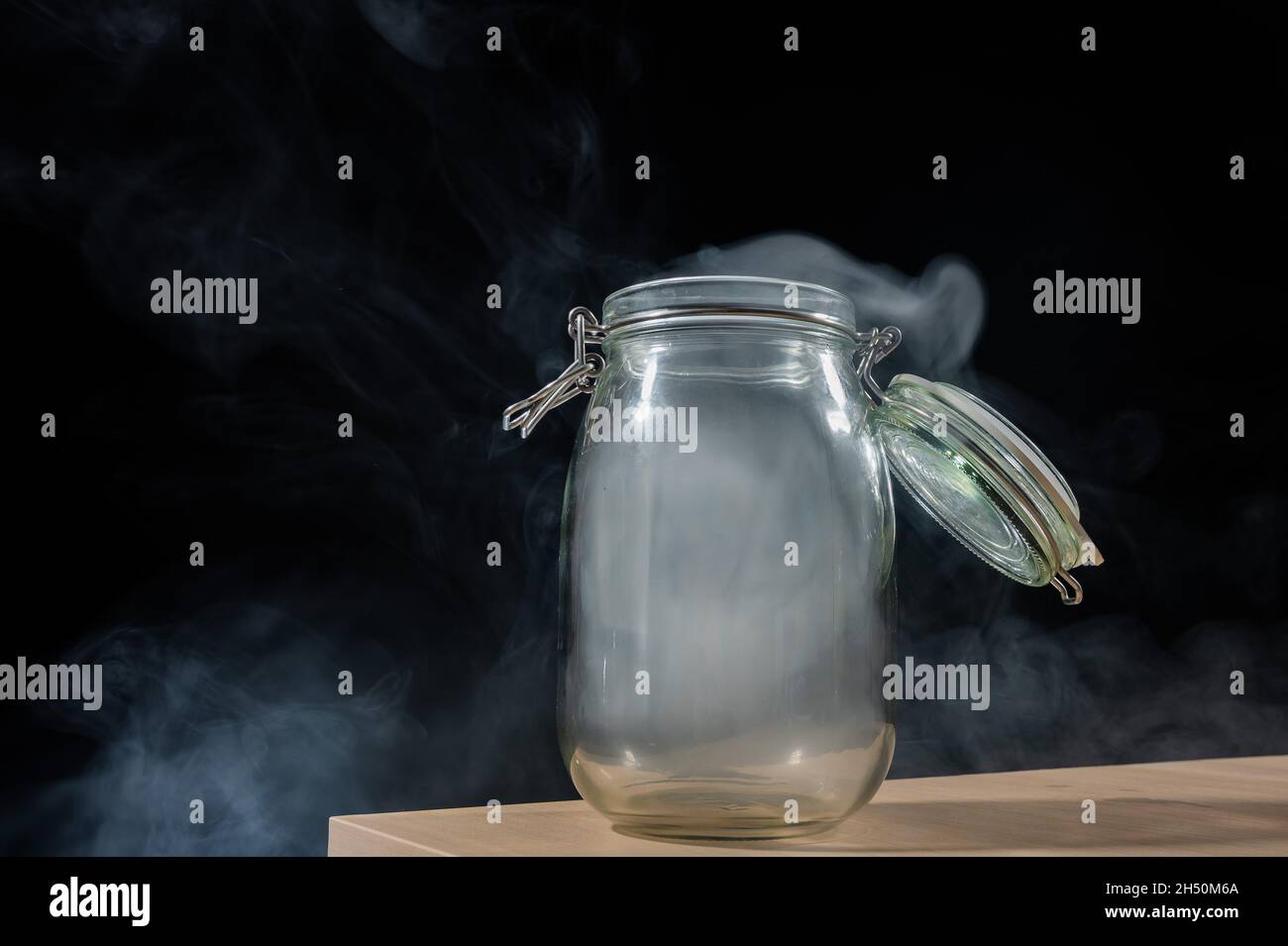 Glass jar with a lid filled with smoke on a black background. Fog in a ...