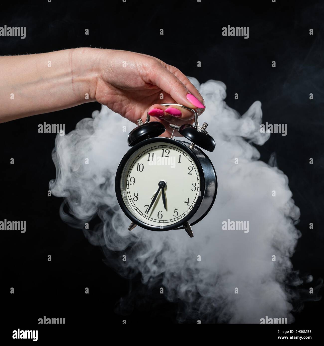 A woman holds an alarm clock in a studio full of smoke. White fog ...