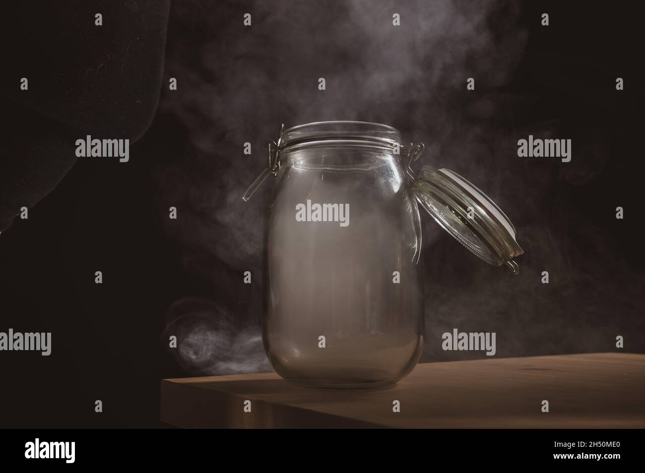 Glass jar with a lid filled with smoke on a black background. Fog in a ...
