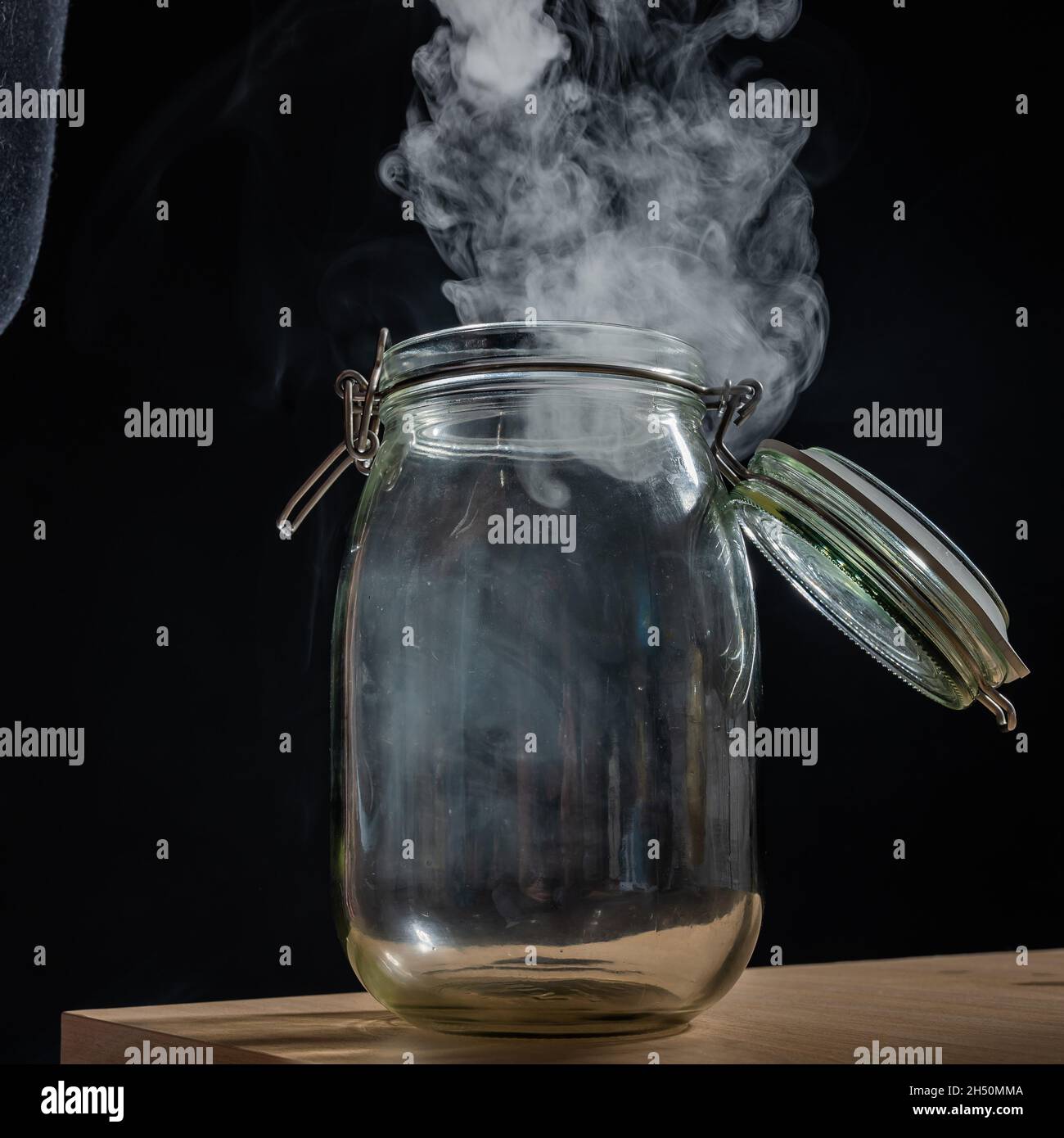 Glass jar with a lid filled with smoke on a black background. Fog in a ...