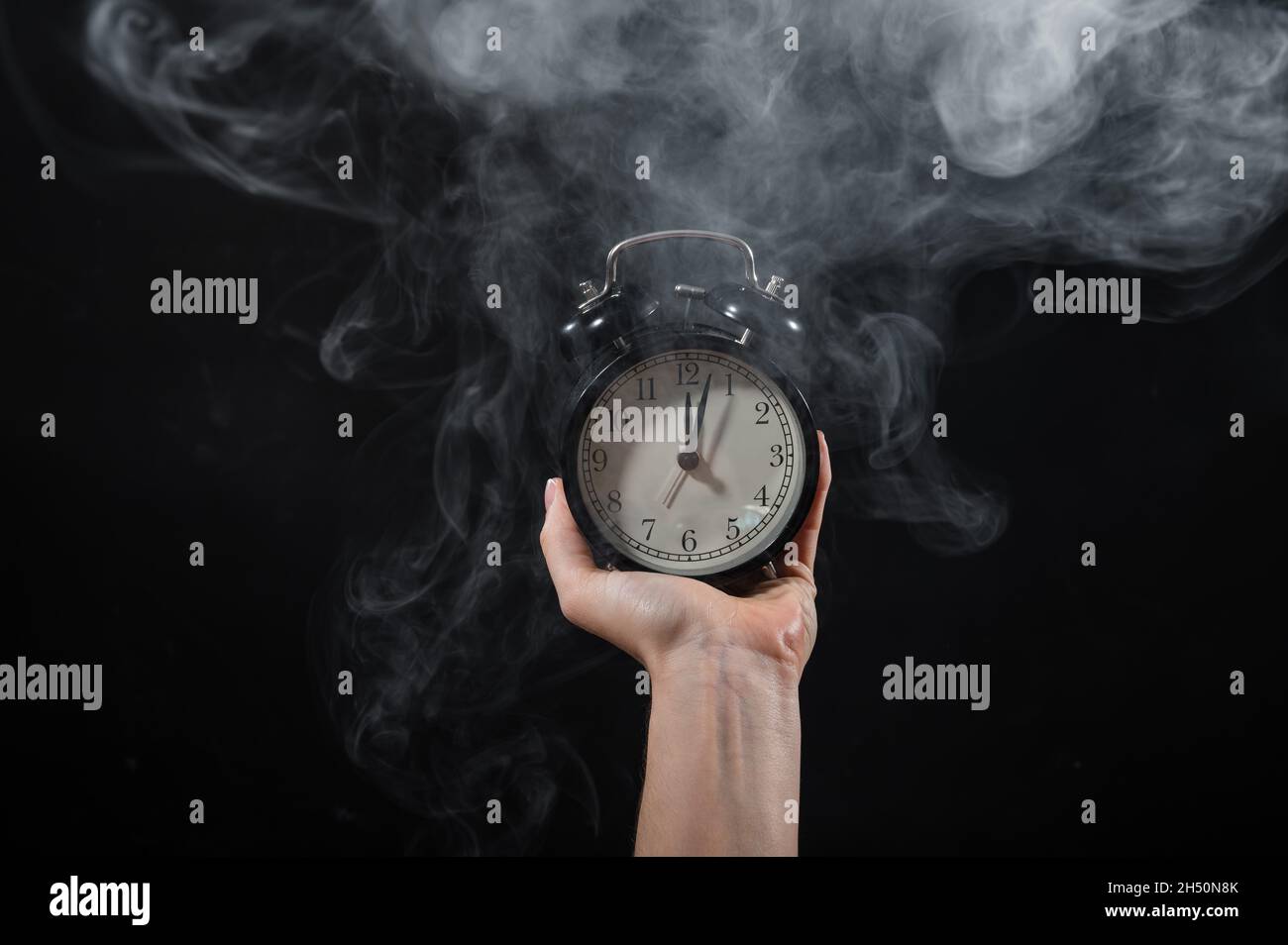 Close-up of a female hand holding a clock on a black background in ...