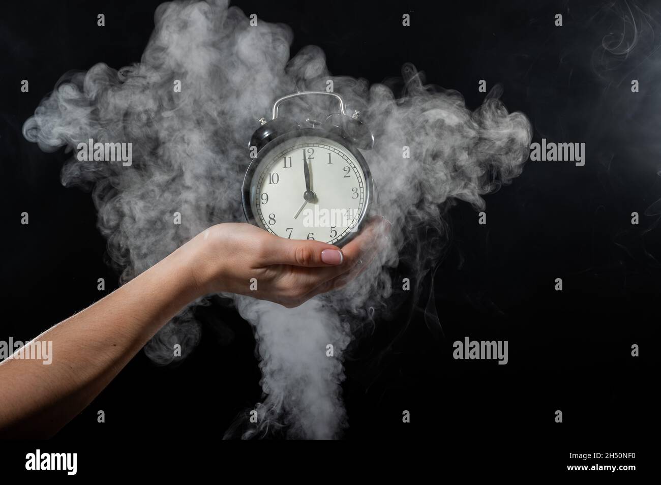 Close-up of a female hand holding a clock on a black background in ...