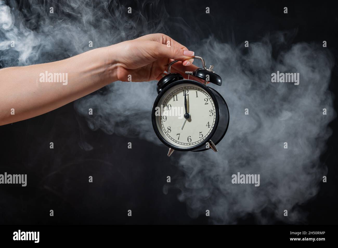Close-up of a female hand holding a clock on a black background in ...