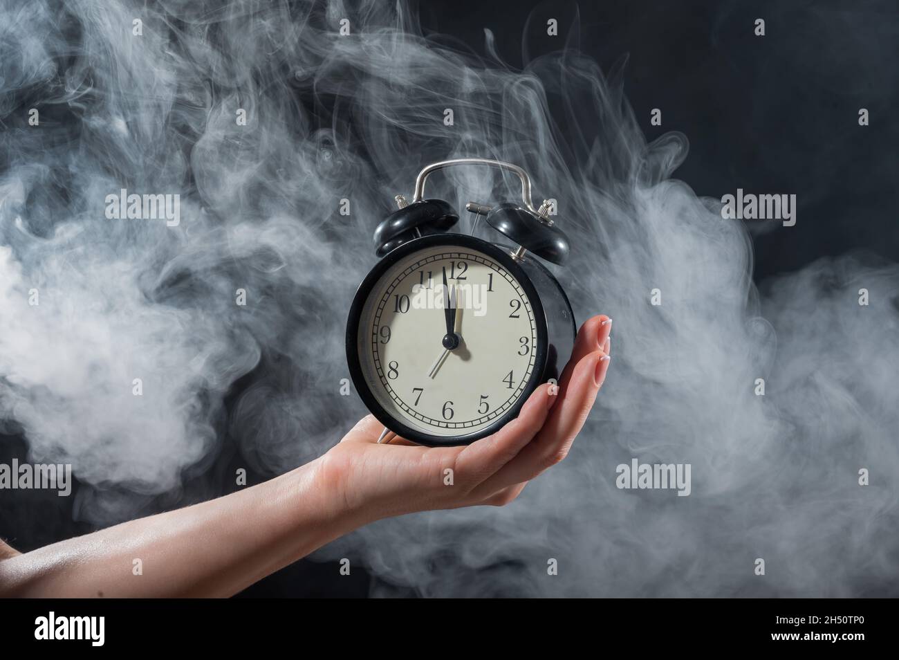 Close-up of a female hand holding a clock on a black background in ...