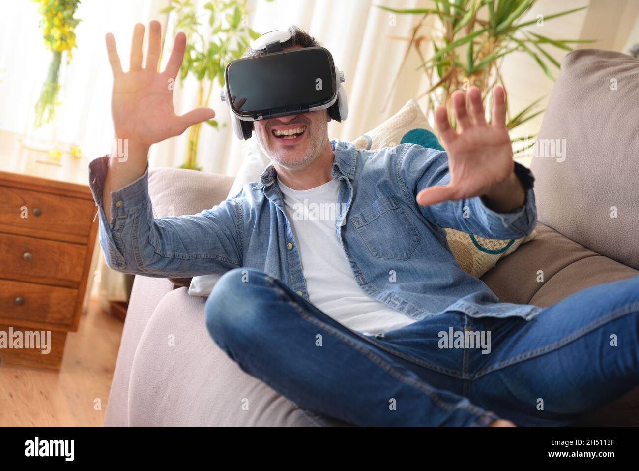 Man using virtual reality glasses lying on a sofa in the living room at ...