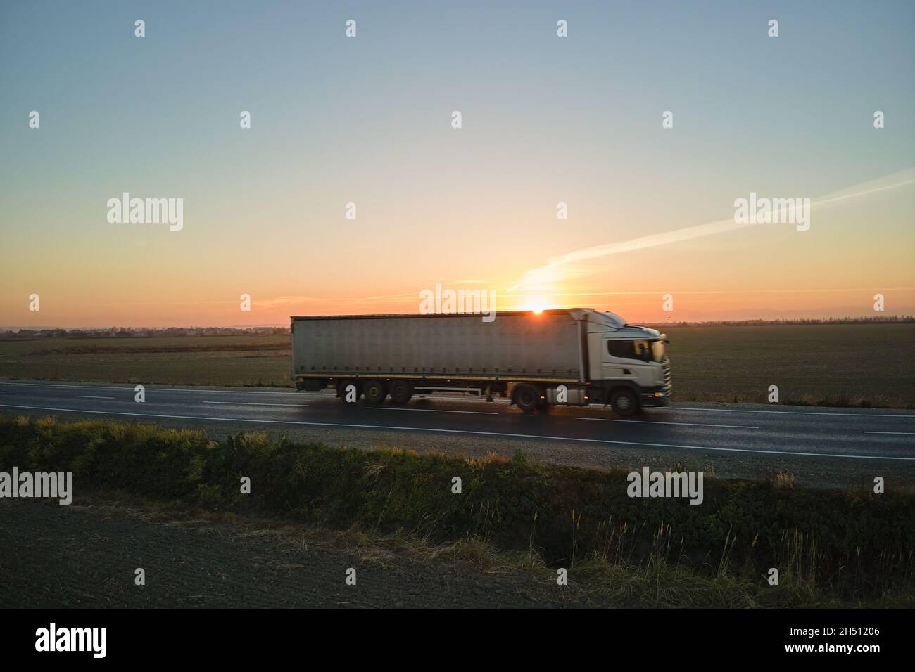 Aerial view of blurred fast moving semi-truck with cargo trailer driving on highway hauling ...