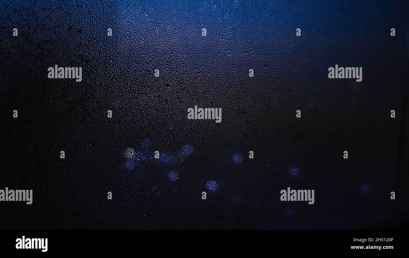 Close-up of window with raindrops on blurred background of lights ...