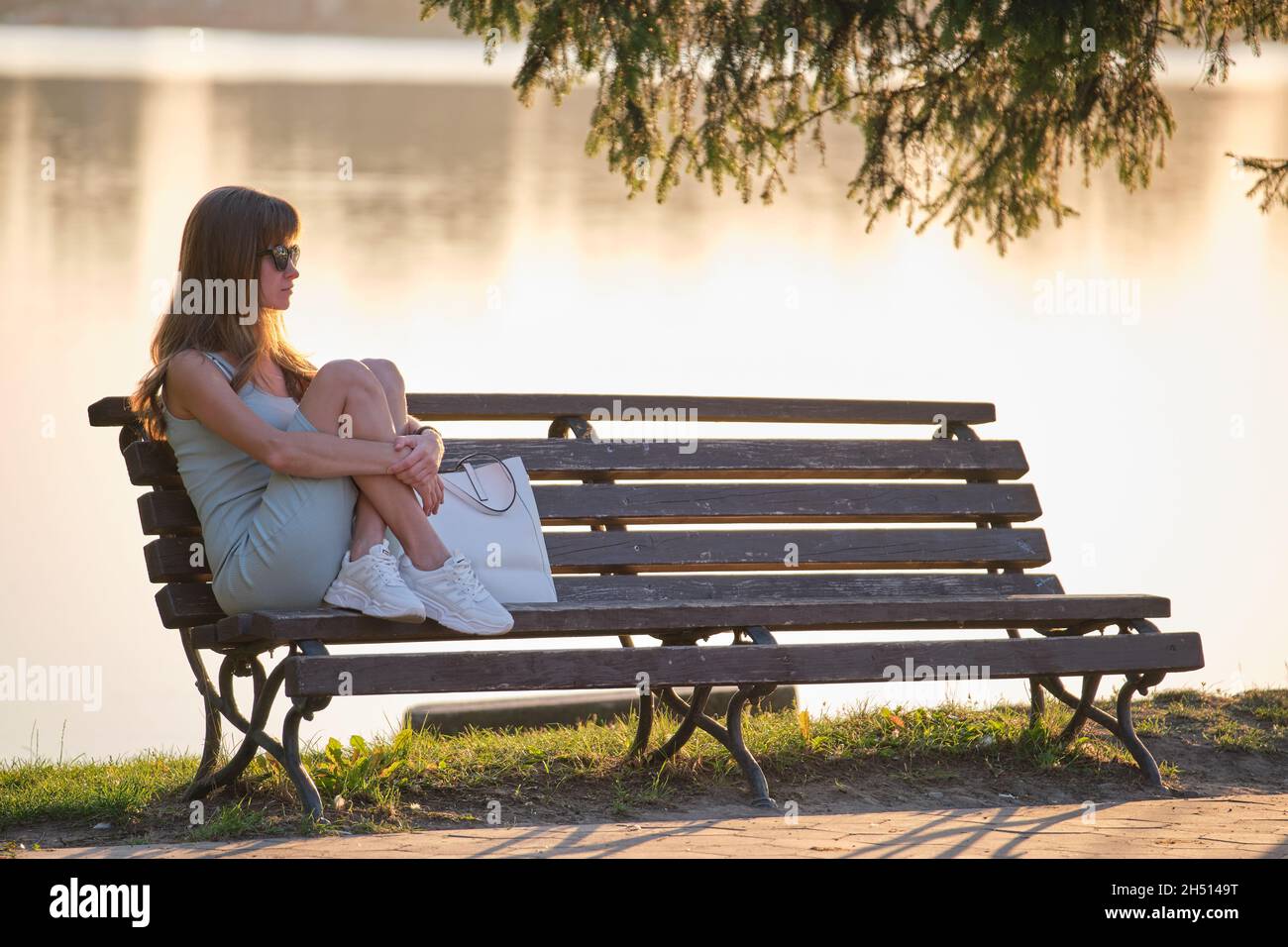 Lonely woman sitting alone on lake shore bench on warm summer evening ...