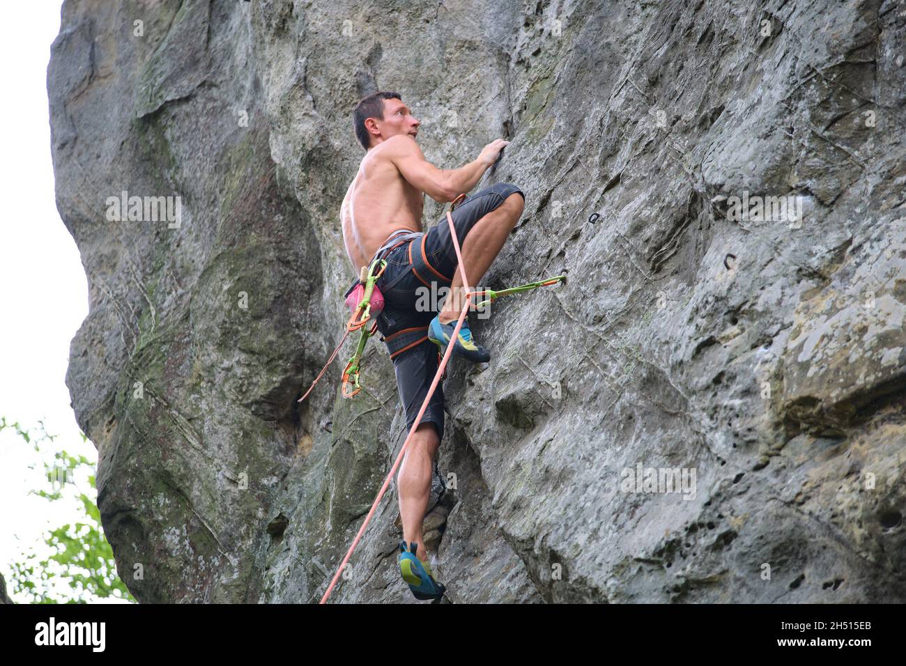 Young man climbing steep wall of rocky mountain. Male climber overcomes ...
