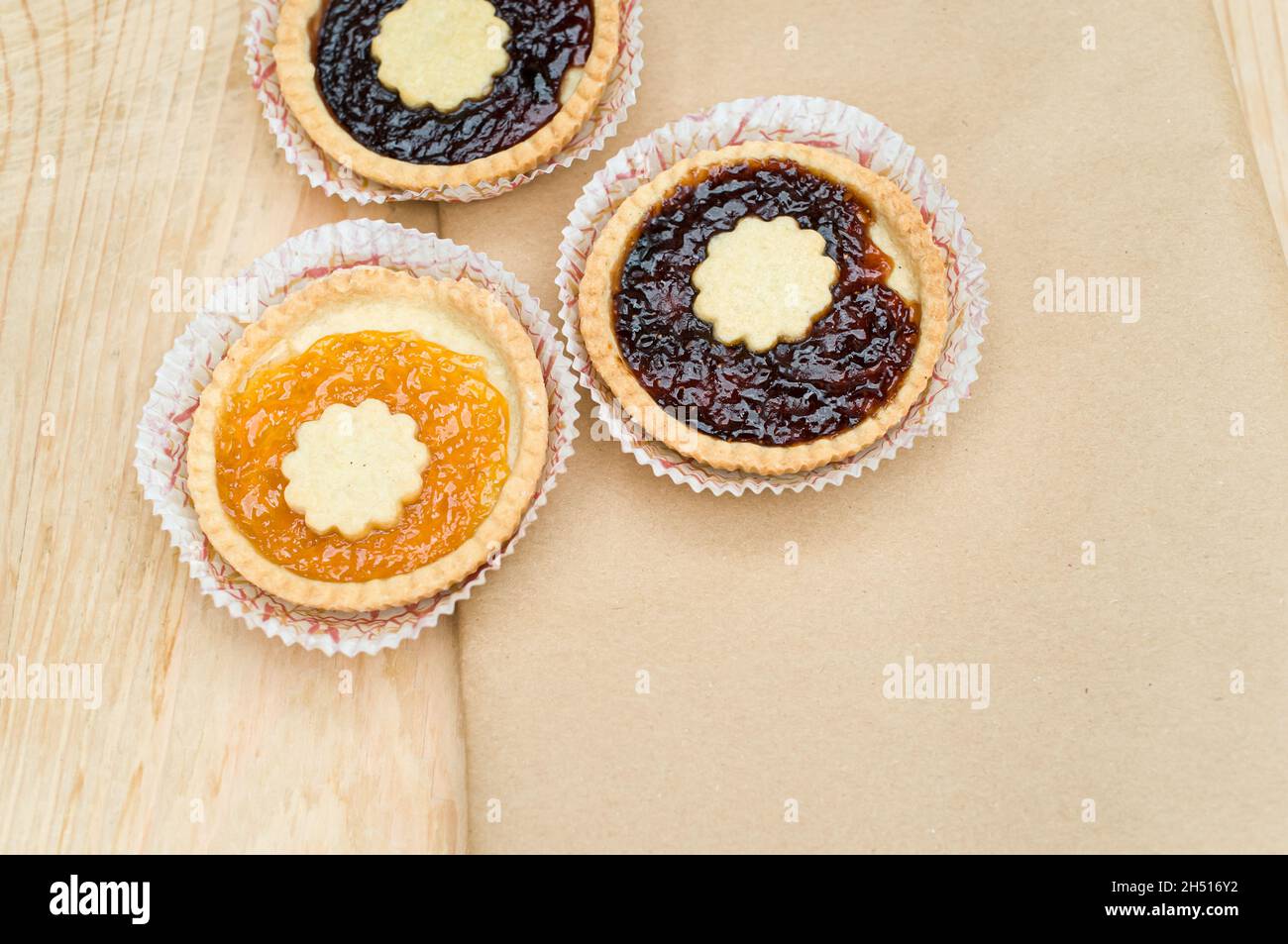 short crust pastry with jam on a food paper and rustic wooden tabletop ...