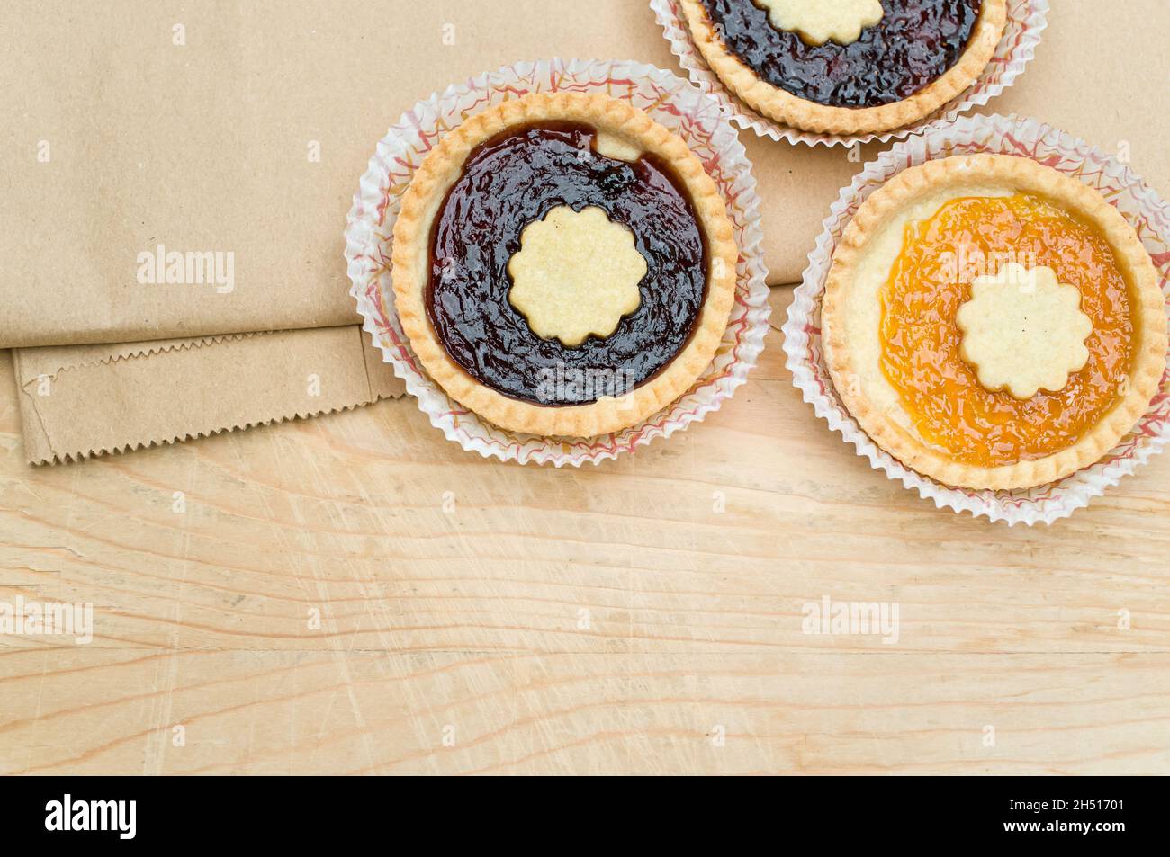 short crust pastry with jam on a food paper and rustic wooden tabletop ...
