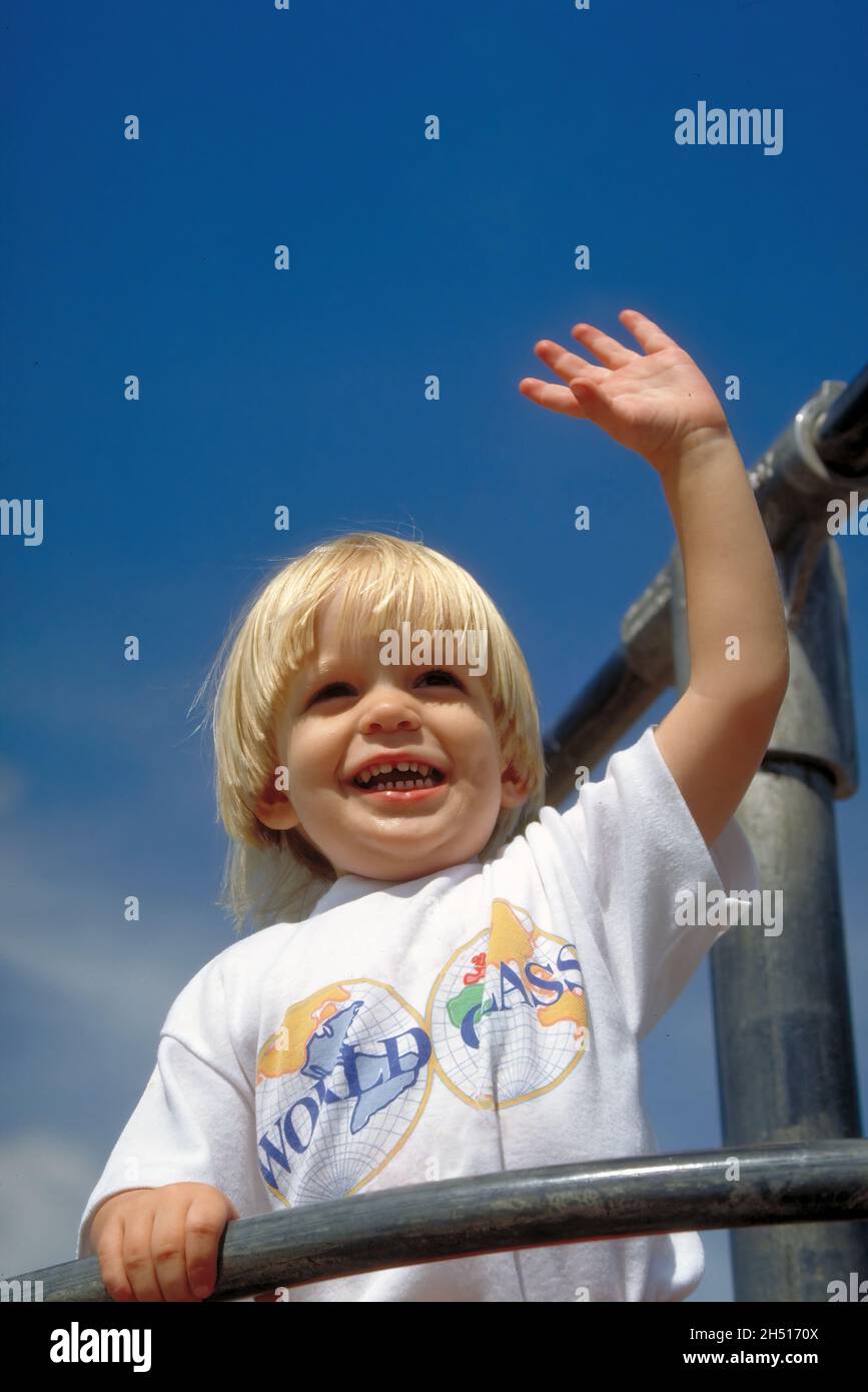 A two to three-year-old toddler waves and smiles from the top of ...
