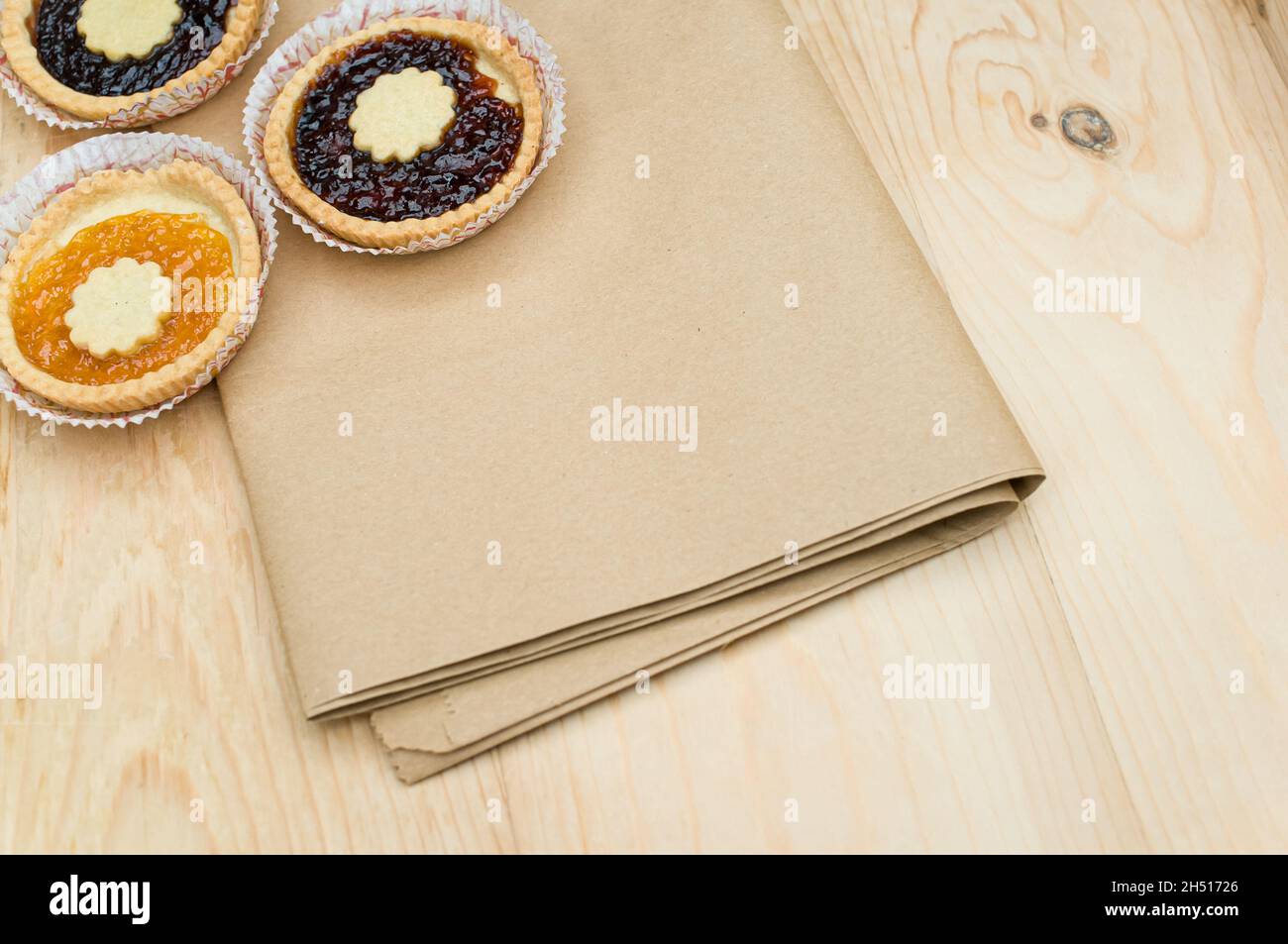 short crust pastry with jam on a food paper and rustic wooden tabletop ...