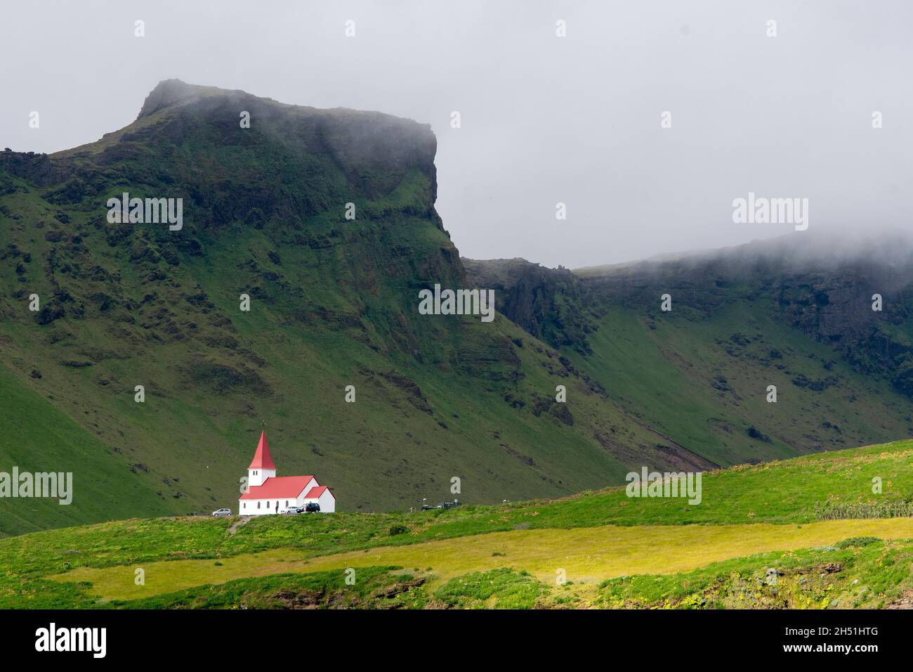 Landscape of Vik i Myrdal church on hill with grassy cliffs in Vik ...