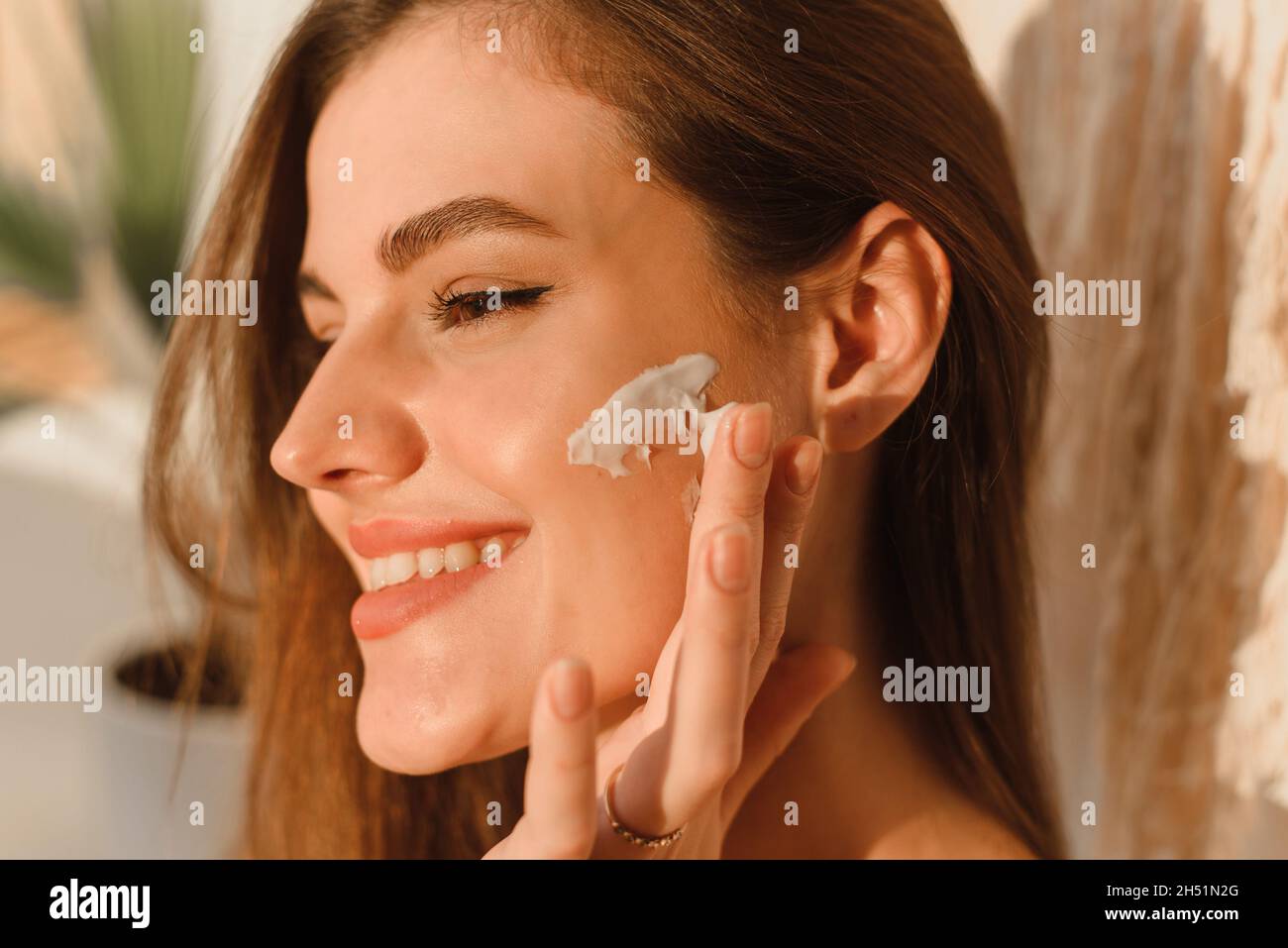 A young woman applies moisturizer to her face in her sun bath. Daily ...