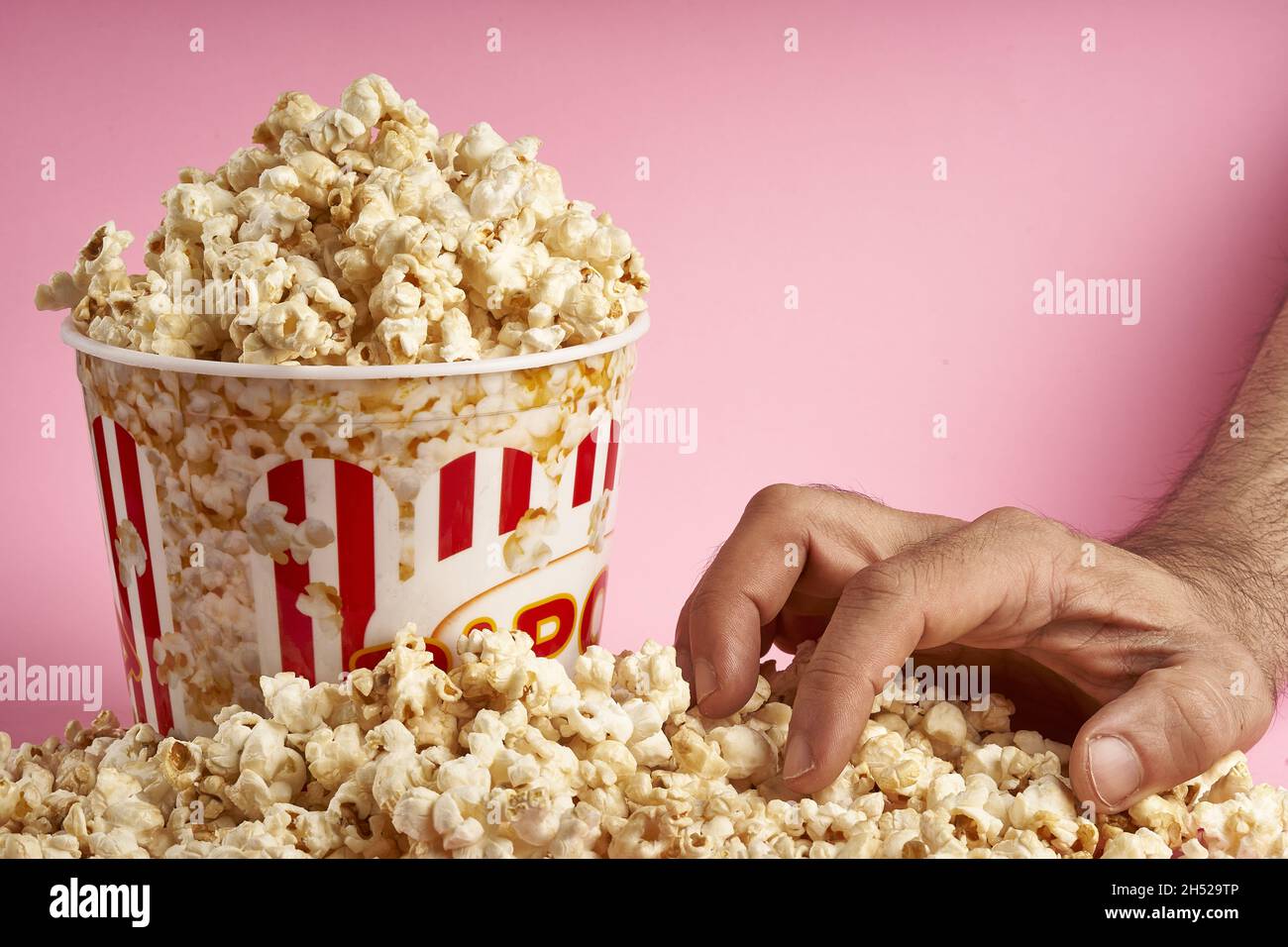 Man's hand holding popcorn and bucket of candy popcorn on pink ...