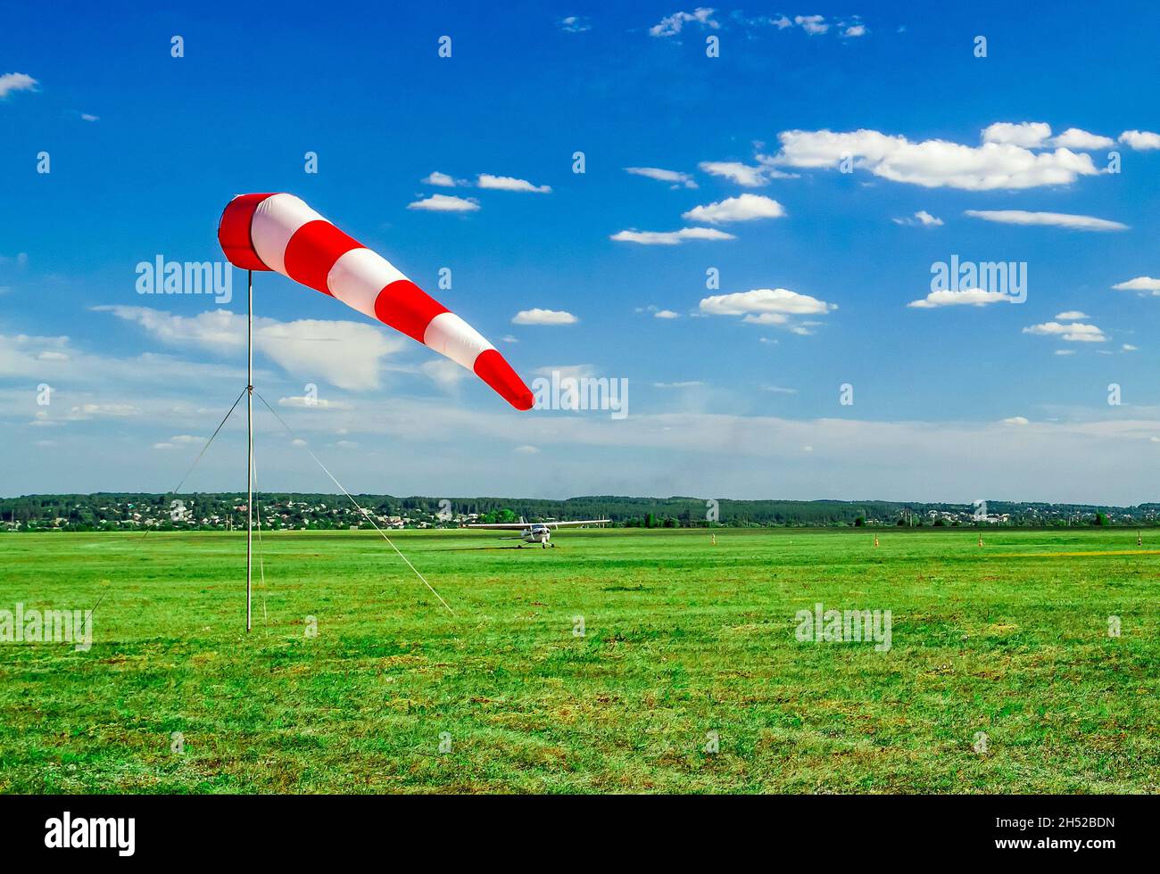 Red and white windsock wind sock on blue sky, green field and clouds ...