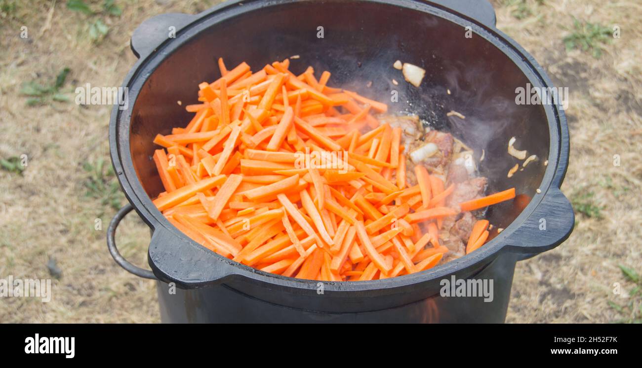Cooking pilaf in a cast-iron wok in the open air. Lots of sliced ...