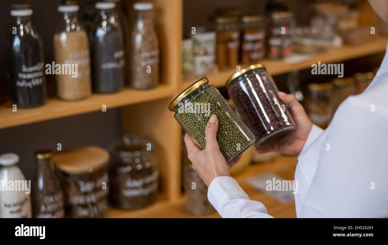 A woman holds glass jars of cereals in an eco friendly store. The ...