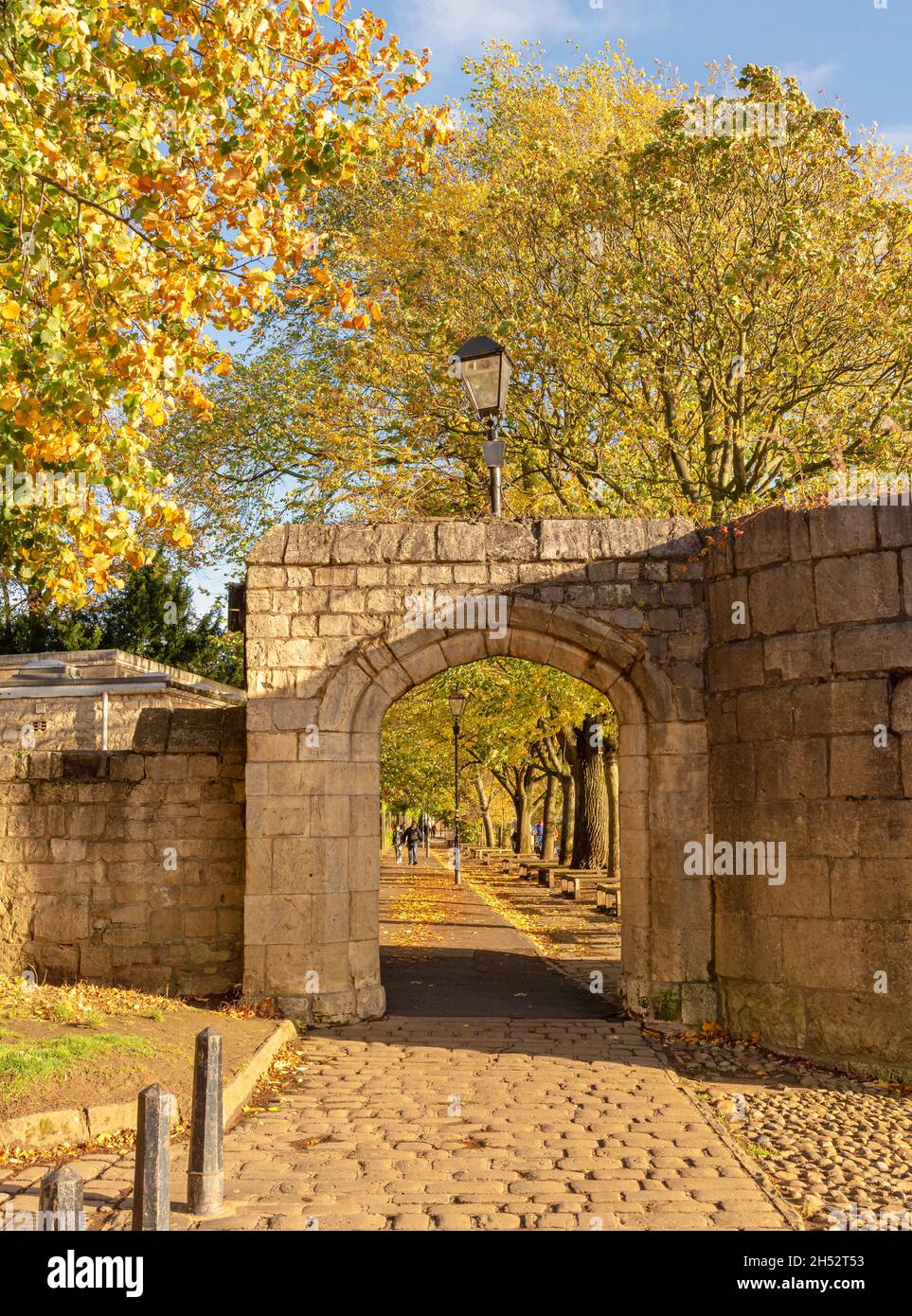 A path runs an arch and a part of a curved historic tower. Autumnal ...