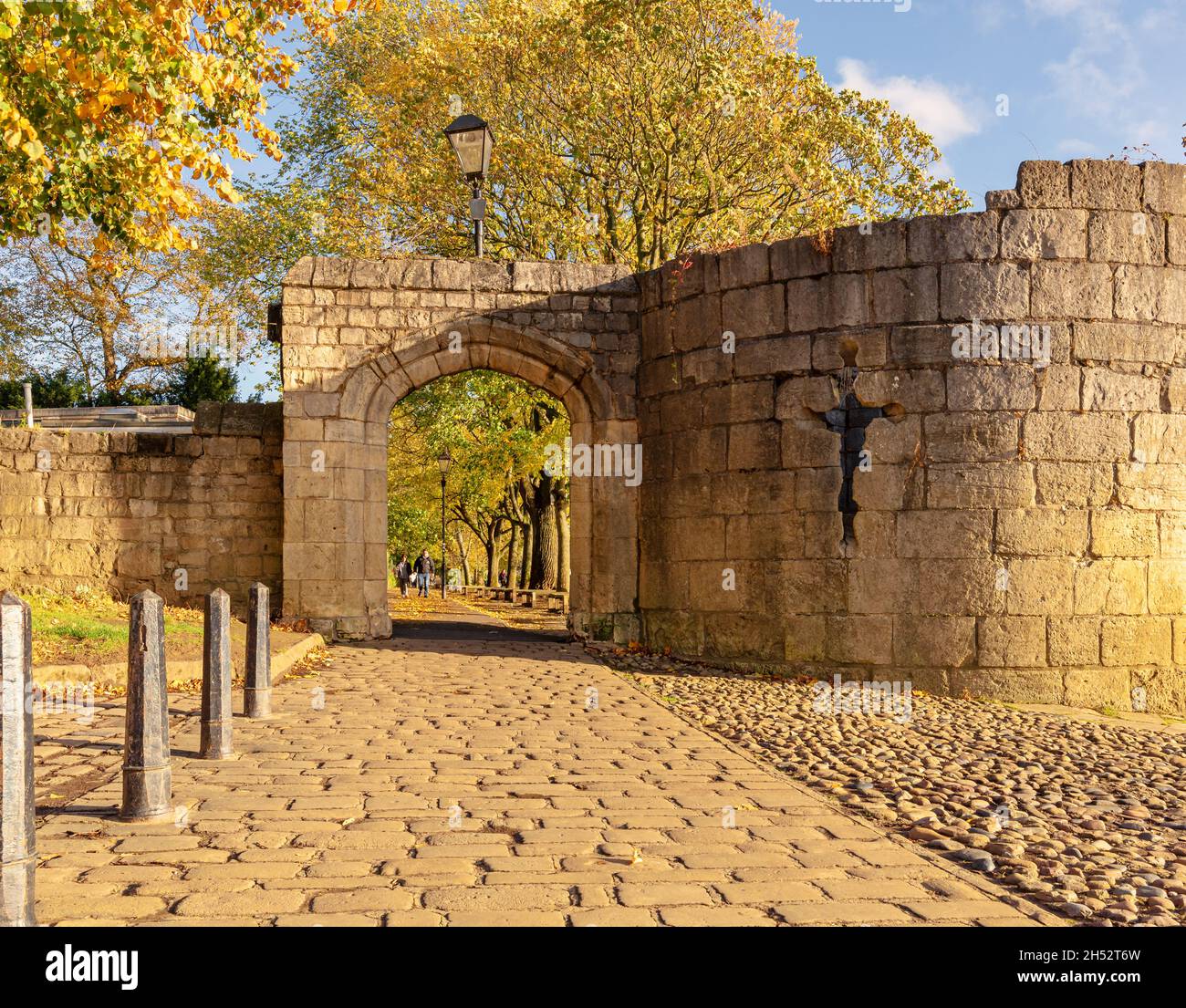 A path runs an arch and a part of a curved historic tower. Autumnal ...