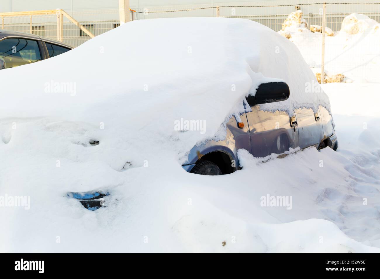 old abandoned broken car parked by the road under a large layer of snow ...