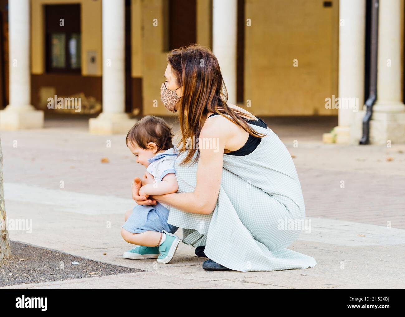 Middle-aged young mother woman crouching in the park with her one-year ...