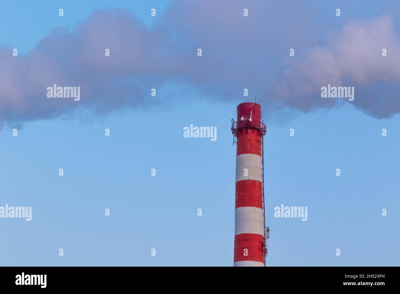 red and white chimney of a factory, from which gray smoke comes out ...