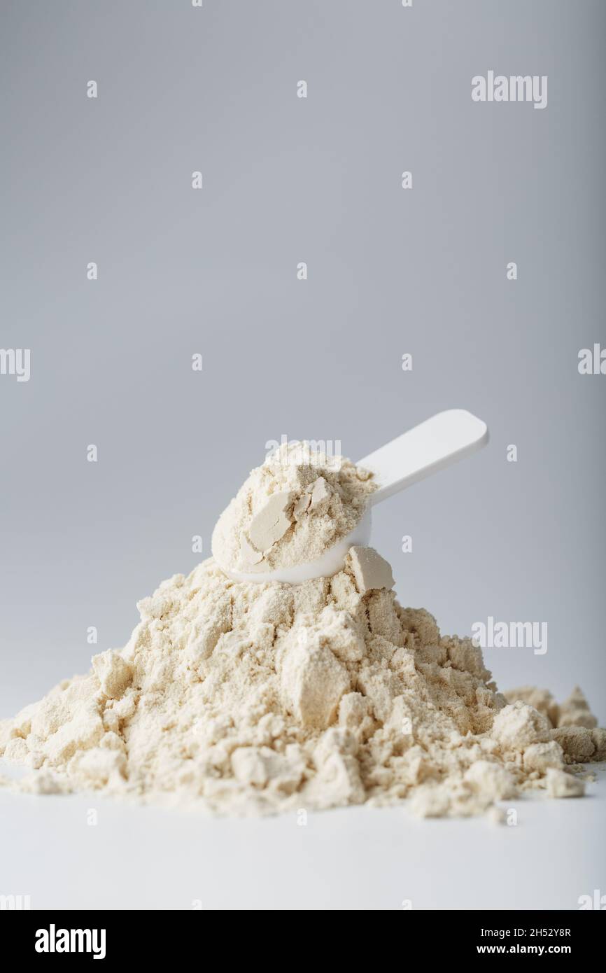 A pile of protein powder with a measuring spoon on a white background ...