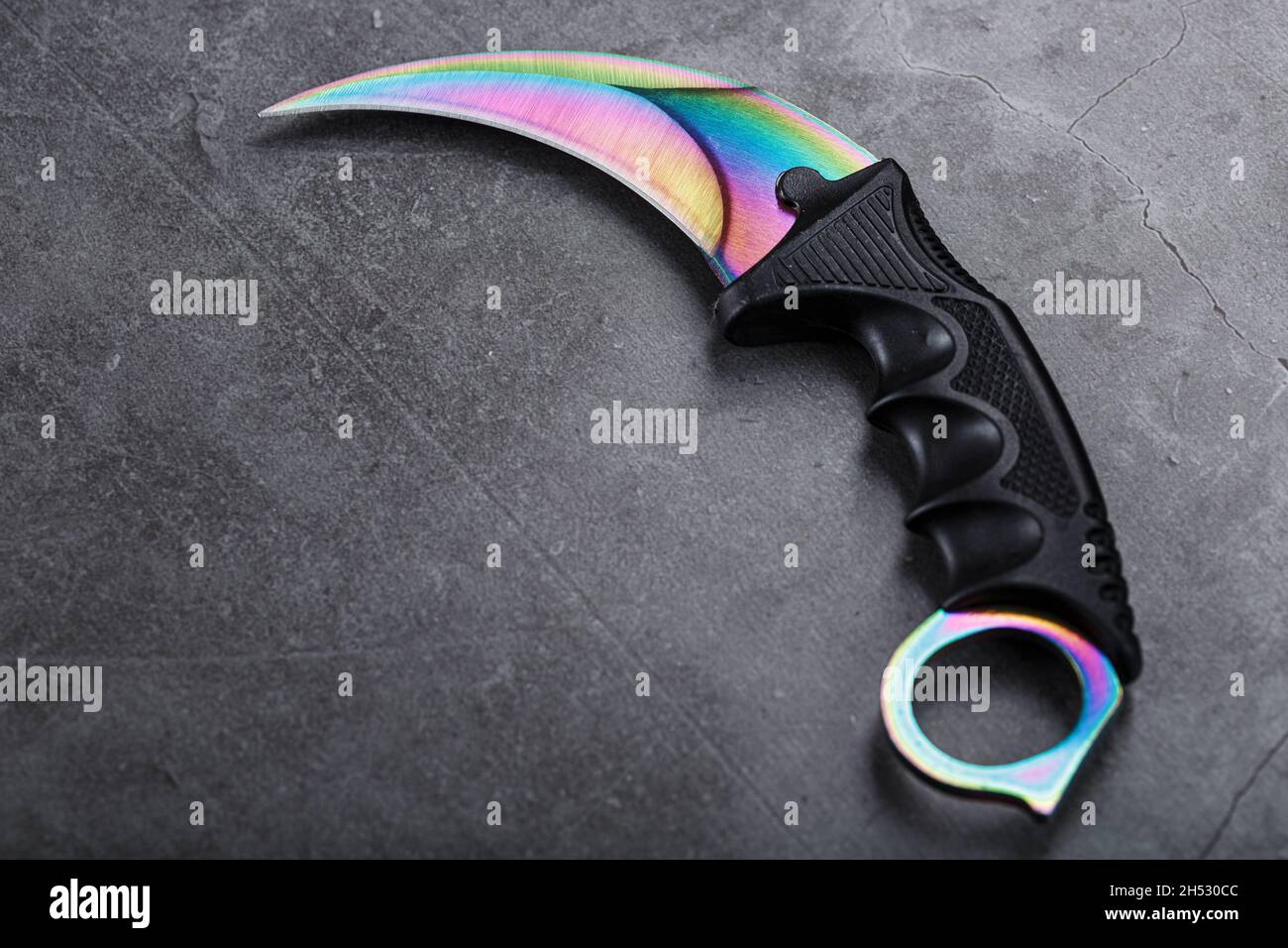 Kerambit dagger with a rainbow-colored blade on a dark textured ...
