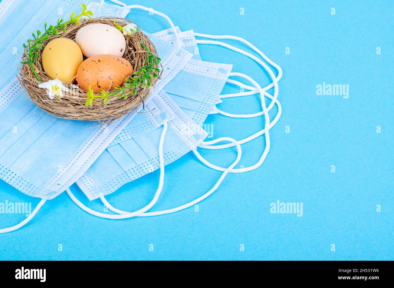 Nest with brightly dyed eggs with medical masks on blue background ...