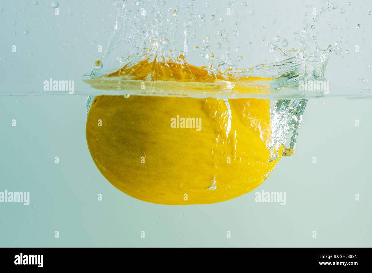 Close up view of melon falling into water on turquoise background ...