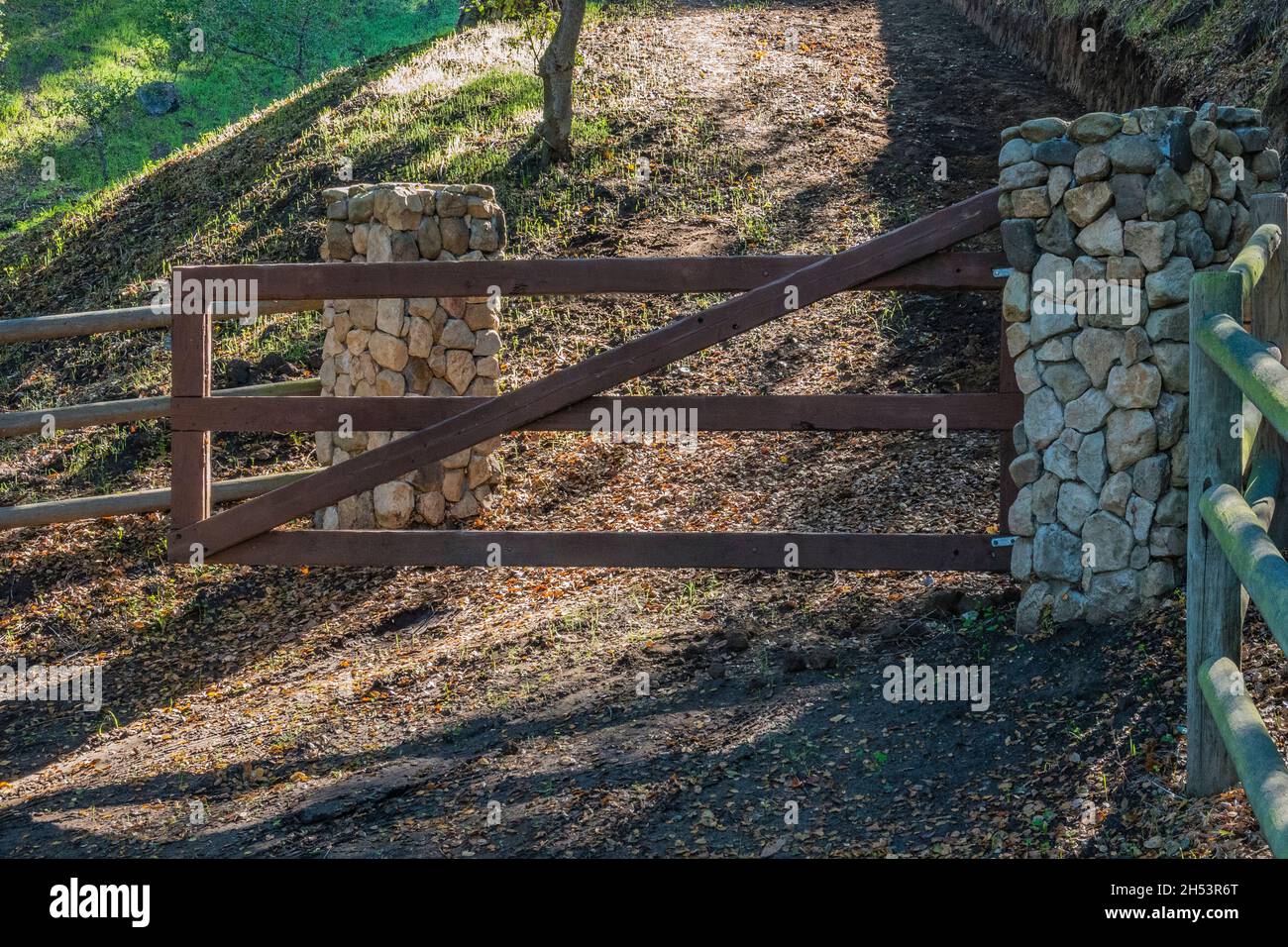 An open wooden gate in rustic setting with rock columns and strong ...