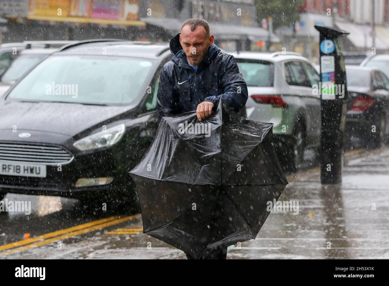 A man struggles to hold an umbrella during a strong wind and rainfall ...
