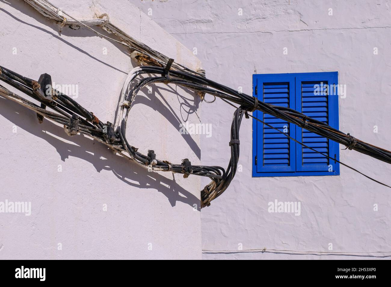 Shot of electric wires attached to a white wall with a blue wooden ...