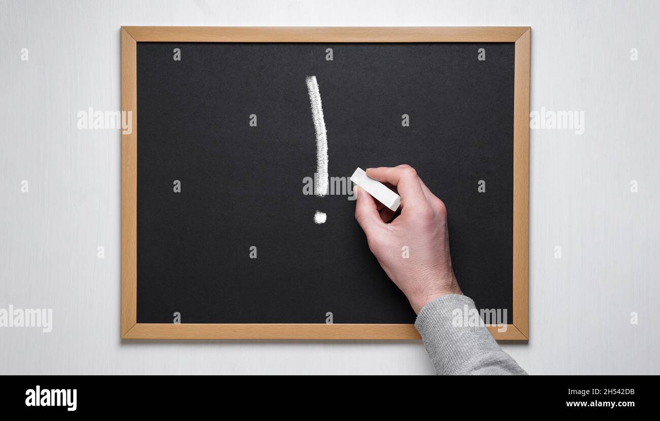 Hand holding chalk on blackboard.Exclamation point on a chalk board ...