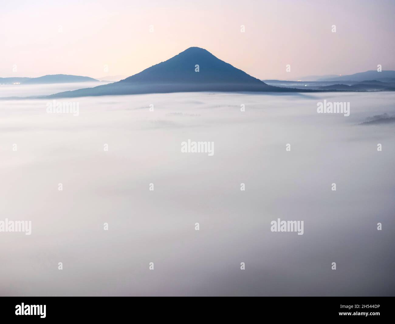 Sharp cone hill growing up from misty flat land. Magnificent foggy ...