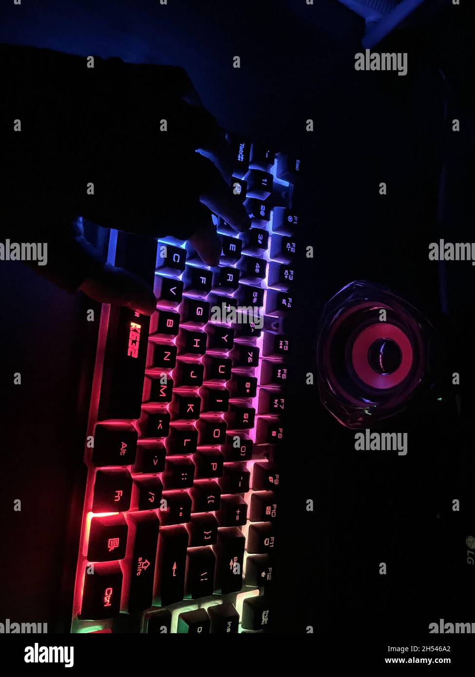 Vertical shot of a hand typing on an illuminated with colorful lights ...