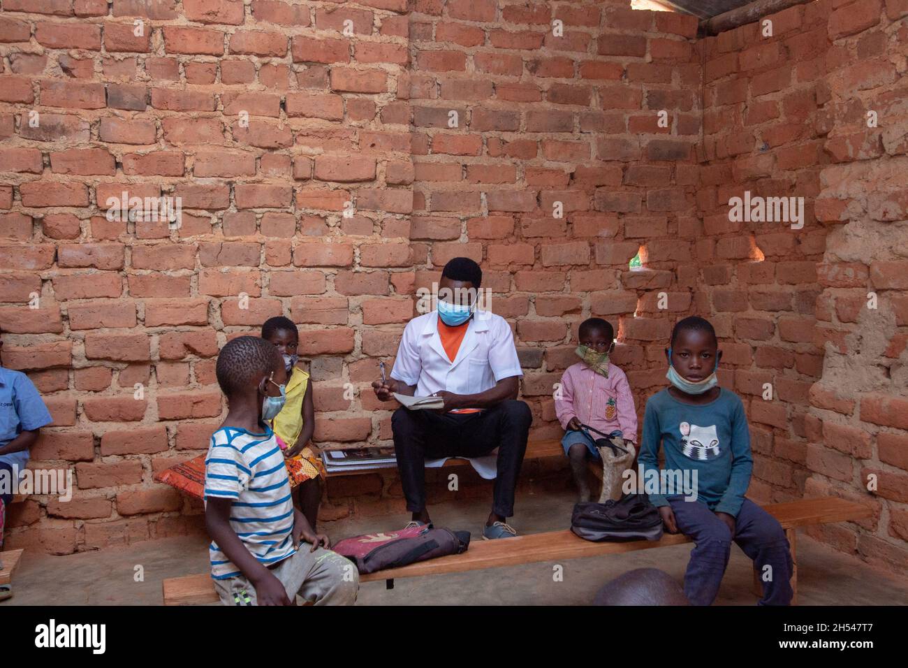 Teacher checking homework in a mud brick classroom, with students ...